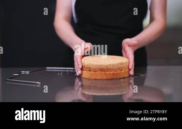 Professional confectioner in black apron connecting cut cake layers ...