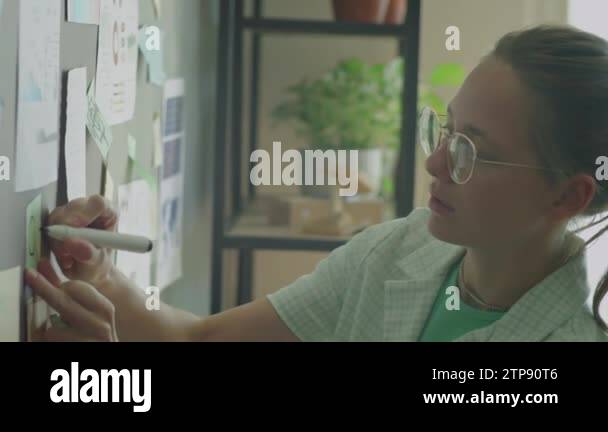 Medium close up shot of gen Z girl writing business ideas on sticky ...