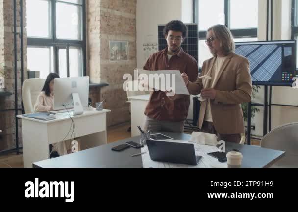 Zoom shot of biracial and Caucasian male engineers standing at table in ...