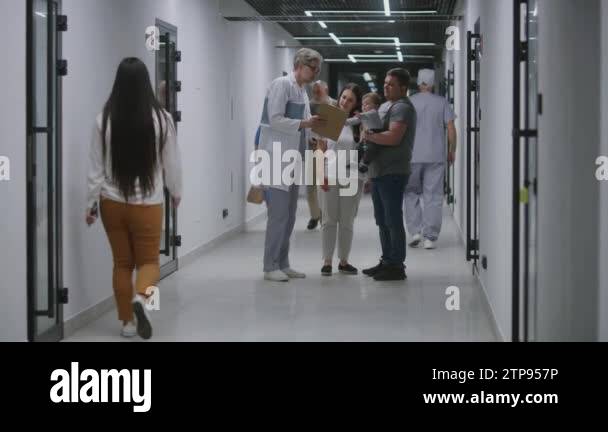 Doctor and family with little child stand in clinic corridor. Doctor talks to patients ...