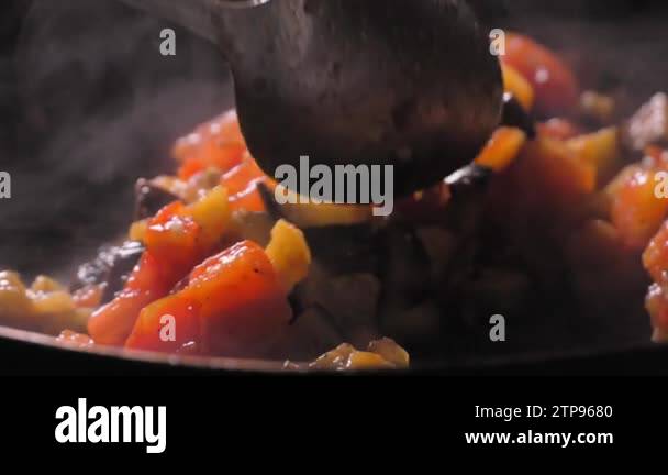Cooking roasted vegetables. Chef stirs with spoon into steaming hot pan ...