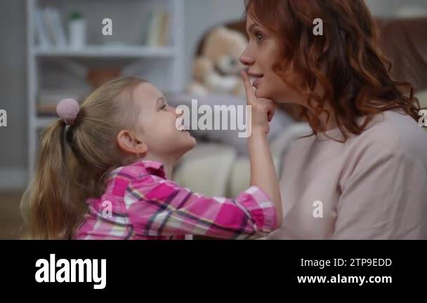 Positive woman talking as girl covering lips with finger and lady ...