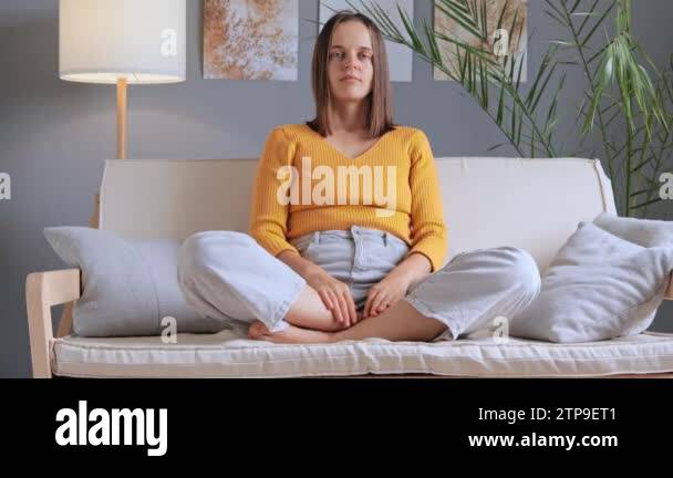 Relaxed woman meditating in her living room at home sitting in lotus ...