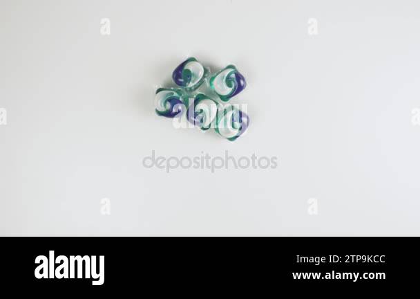 Five washing powder pods on a white table. Child s hand takes one ...