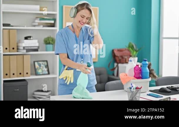 Young blonde woman professional cleaner cleaning table listening to ...