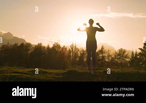 SILHOUETTE, LENS FLARE: Athletic lady raises arms on mountaintop at ...