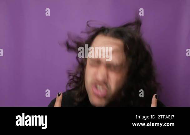 Young handsome punk guy shakes his long hair and shows the goat sign ...