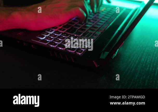 A mans hand types on a laptop keyboard backlit in neon light Stock ...