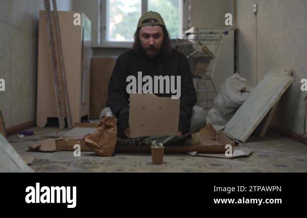 Homeless poor man sitting in a room of an abandoned building. He is ...