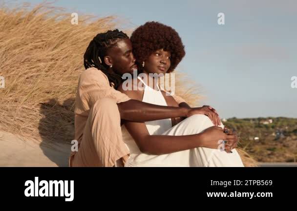 A stylish black African couple, in a romantic moment, sits on a sandy ...