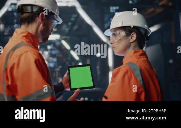 Engineer teaching woman intern on factory showing green screen tablet close up. Skilled ...