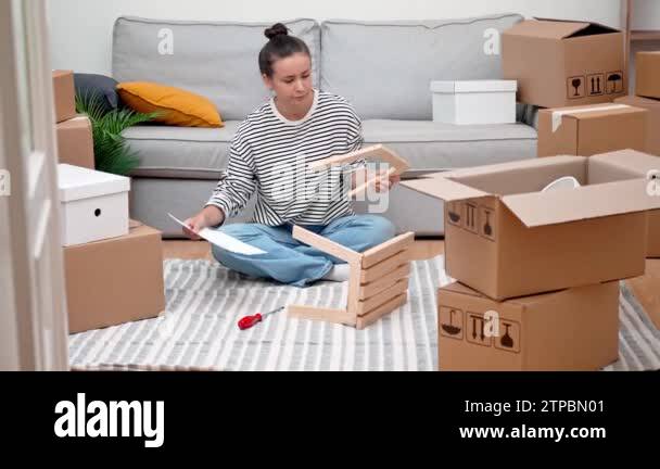 woman, sitting on the floor of her new house, assembles a self-assembly ...
