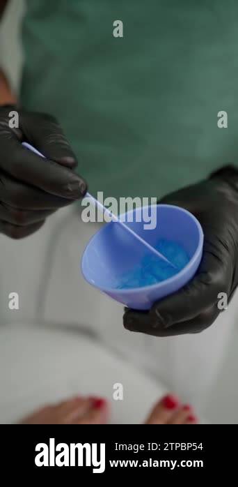 Professional beautician in gloves using a sterile wand to obtain melted wax for depilation from ...