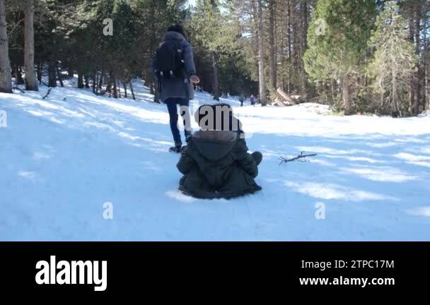 Woman in warm winter clothes running and pulling happy kids on sled ...