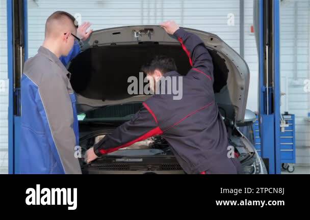 Two young caucasian mechanics open engine compartment at the car ...