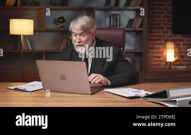 Portrait of older man in formal clothes powering off laptop computer ...