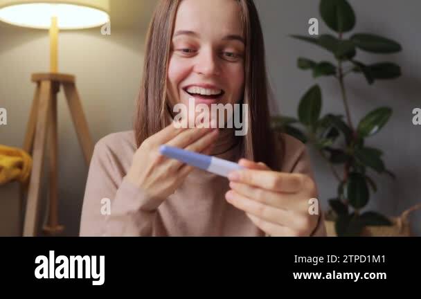 Happy cheerful looking at pregnancy test with two stripes rejoicing ...