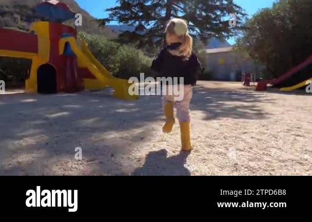 Little girl runs across the playground to the slide and starts to climb ...