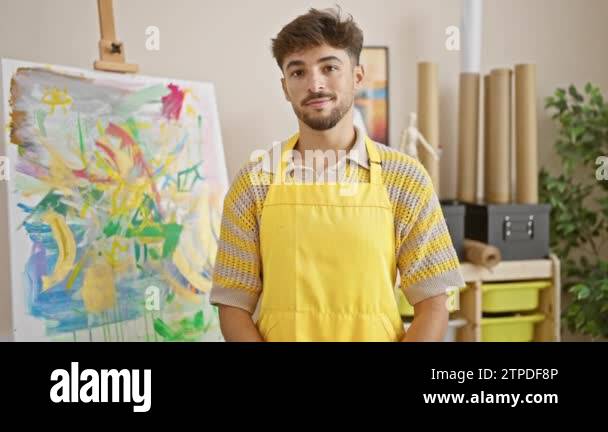 Confident young arab man, arms crossed, smiling at canvas in art studio ...