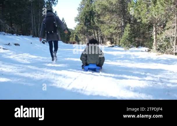 Woman in warm winter clothes running and pulling happy kids on sled ...
