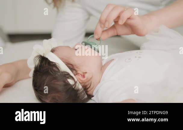 Mother takes away pacifier from child. Newborn baby dressed in cute ...