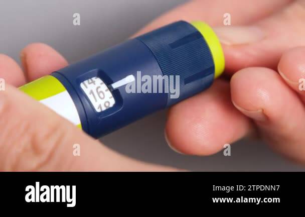 Close up on hands turn knob on insulin pen and dial up insulin dose for ...