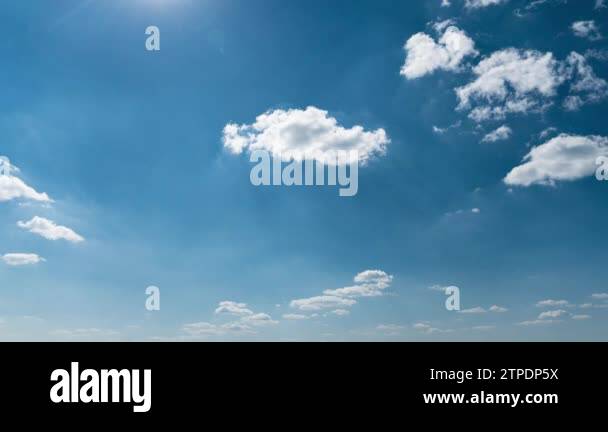 White fluffy clouds slowly float through the blue daytime sky timelapse ...