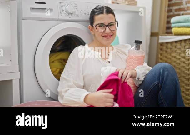 Young beautiful hispanic woman washing clothes holding detergent bottle at laundry room Stock ...