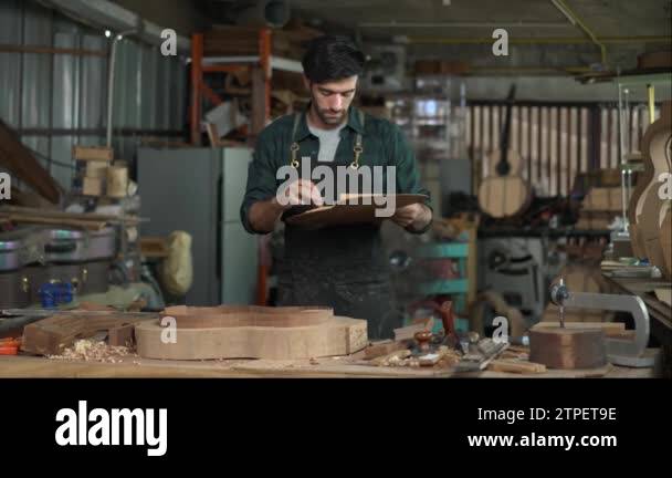A skilled luthier is hard at work sanding the body of an acoustic ...