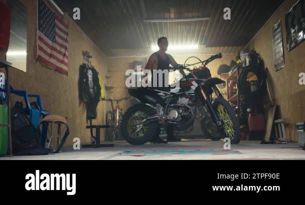 A male mechanic rolls out his motorcycle from his workshop garage with ...