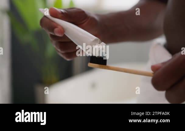 Close up hands squeezing out white toothpaste from tube on toothbrush ...