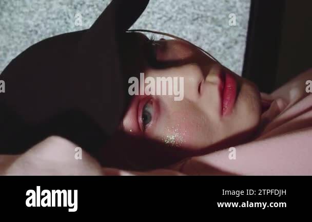 Young tattooed woman lying in front of working static tv set in dark ...
