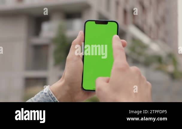 Close Up Of Phone With Vertical Green Screen In Men's Hands On City Buildings Background. Guy ...