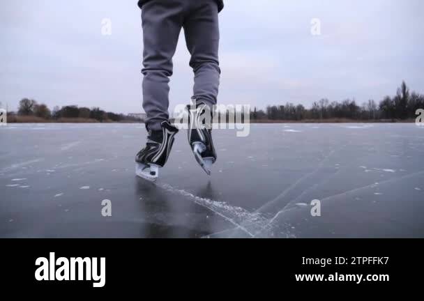 Male legs of skater shod in figure skates sliding on ice rink at nature ...