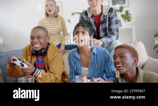 Happy diverse group of teenage friends raising hands and playing video ...