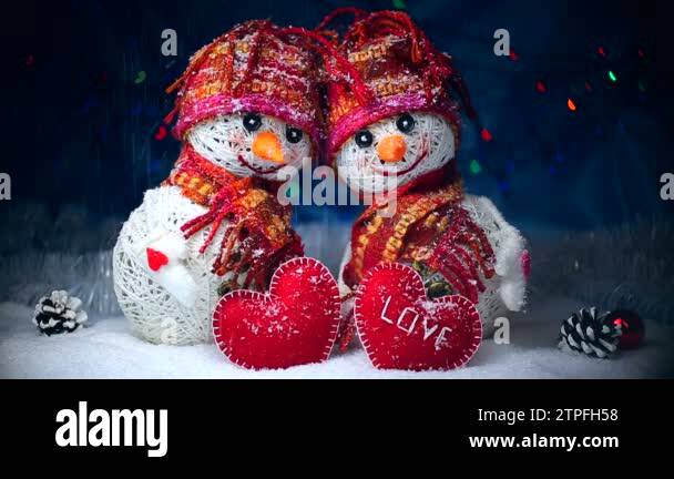 Valentines Day. Snowmen in love stand on the snow and keep their hearts ...