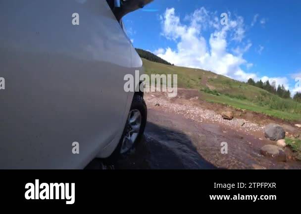 A white SUV drives through the river and mud. View of the wheels. The ...