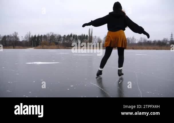 Young girl training rotation skills on frozen river. Woman shod in ...