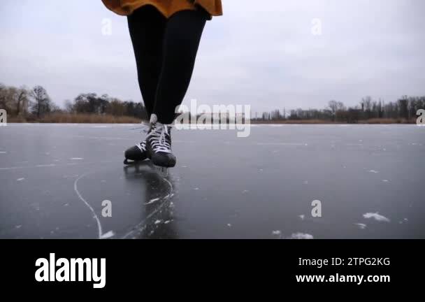 Female legs shod in figure skates sliding backwards on ice rink outdoor ...