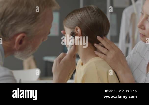 Chest up of professional male otolaryngologist examining ears of Asian ...