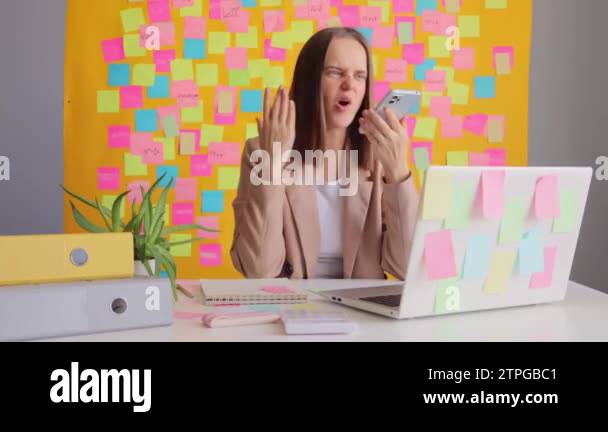 Angry aggressive young woman in jacket holding telephone while sitting ...