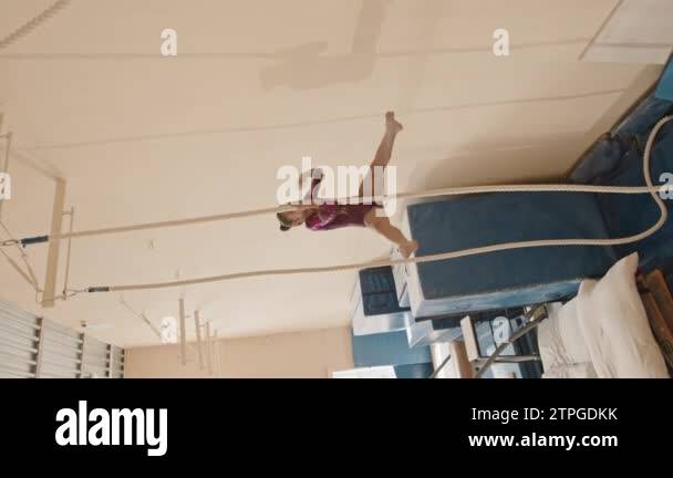 Vertical full length shot of little gymnast girl in leotard climbing up ...