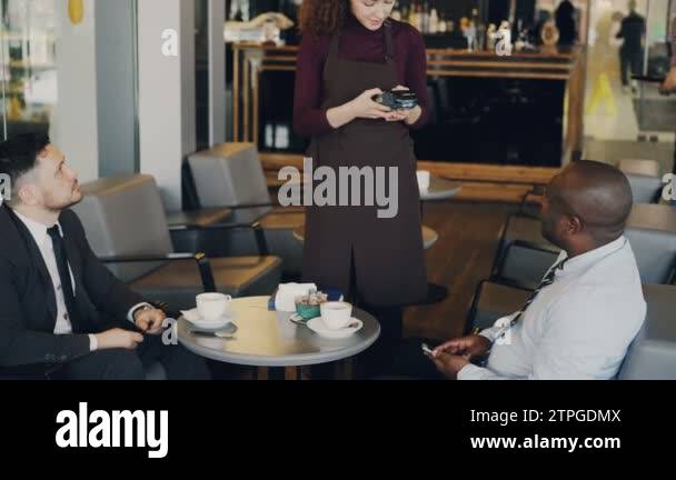 Two multiracial businessmen in formal wear pay online bill using smartphone in modern cafe ...