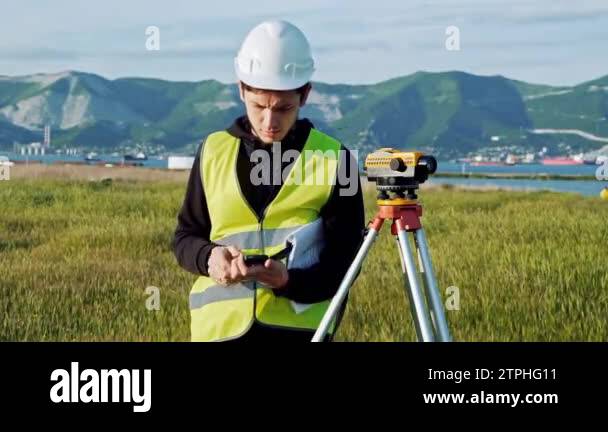 surveyor man in green work clothes and helmet adjusts the equipment ...