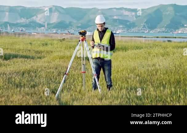 surveyor man in green work clothes and helmet adjusts the equipment ...