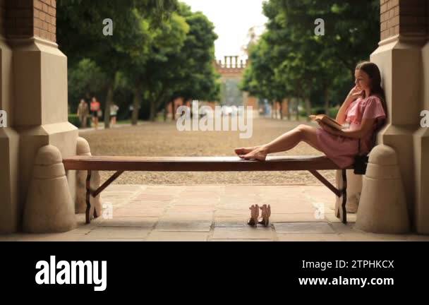 Pretty teenage girl lying down on bench in university campus and ...