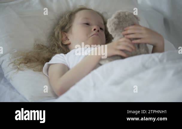Lonely young girl lying in bed and hugging toy, unhappy child missing ...