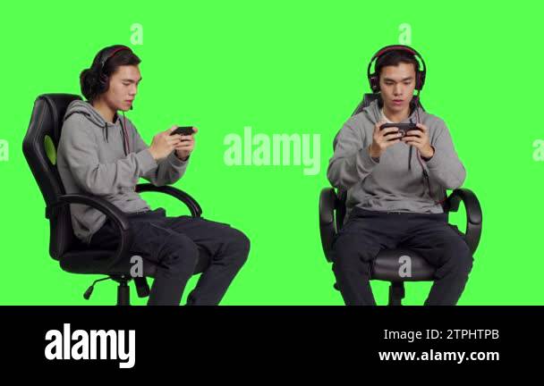 Asian young man plays mobile games over greenscreen, holding smartphone ...