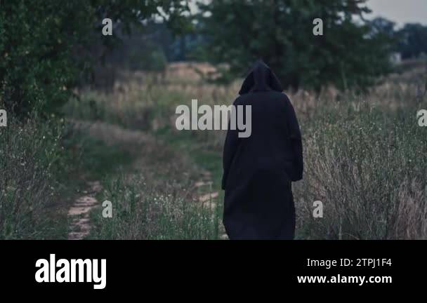 Backside view of witch on the field. Black death goes slowly away along ...