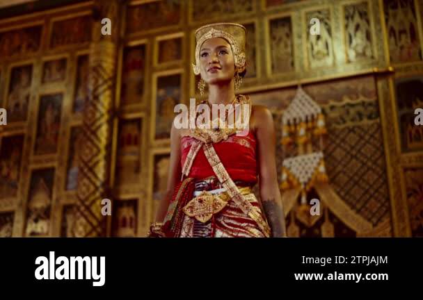 A woman adorned in traditional Thai attire gracefully performs the revered Wai gesture, a symbol ...